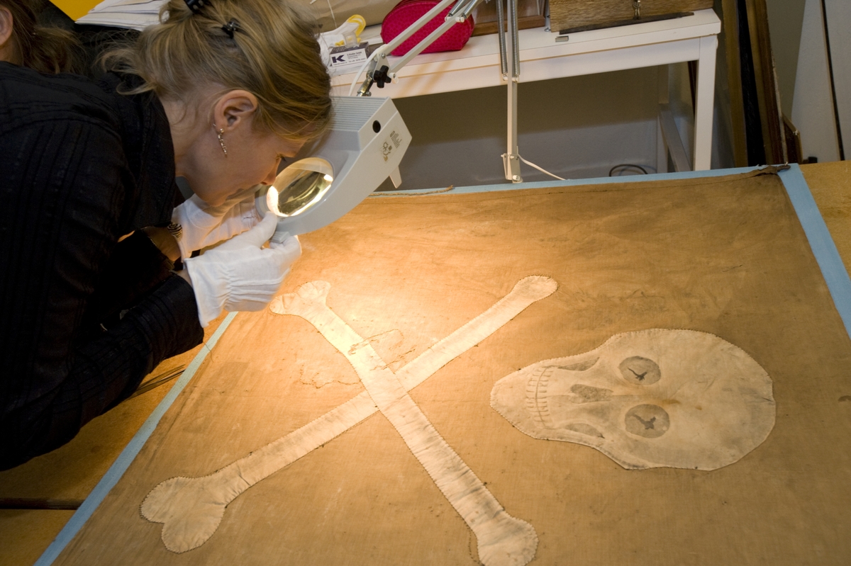 Konservator från Armémuseum tittar till en inlånad piratflagga från ...