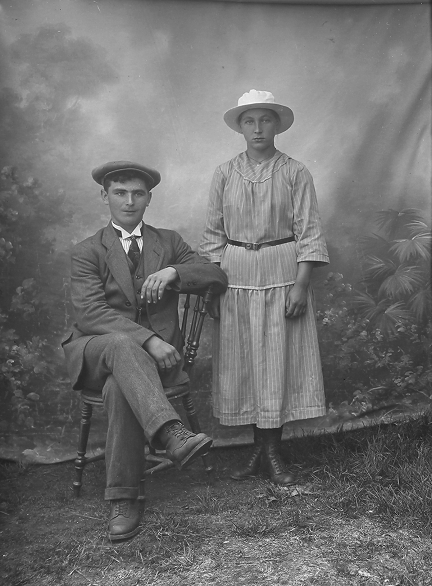Portrett. Par i 20-åra. Mannen sitter. Finklær. Lue/hatt. Bildet er ...