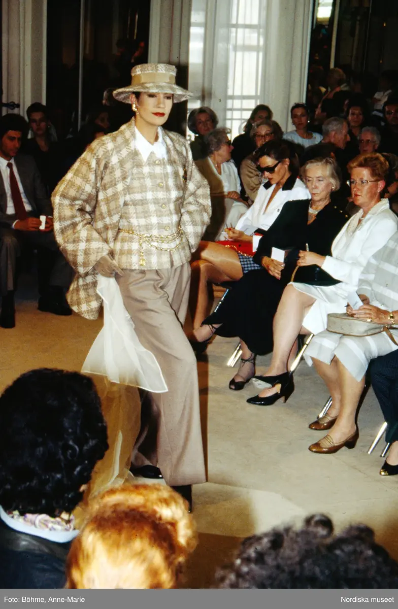 Modevisning. Modell i rutig jacka och hatt, vida byxor i beige ton och ...