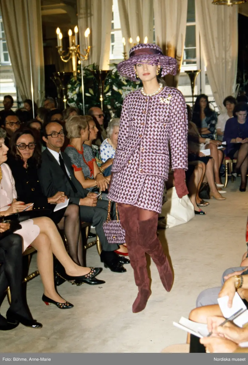 Modevisning. Modell i lila dräkt med matchande hatt och väska och höga ...