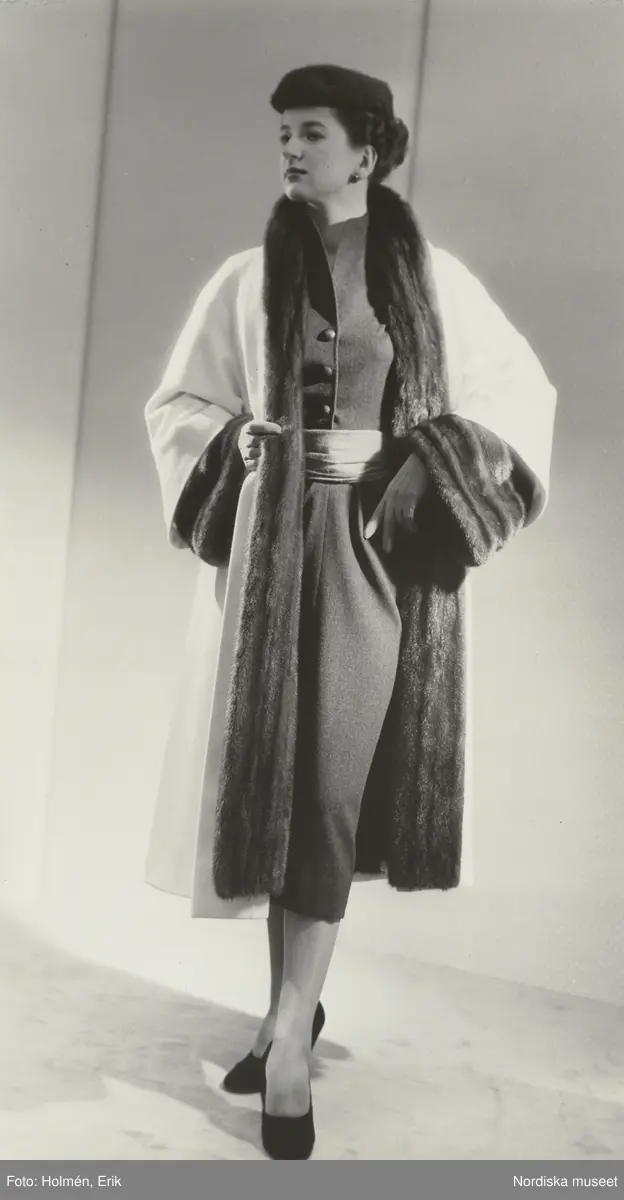 Modell i klänning med band i midjan, ljus kappa med pälskant och ...