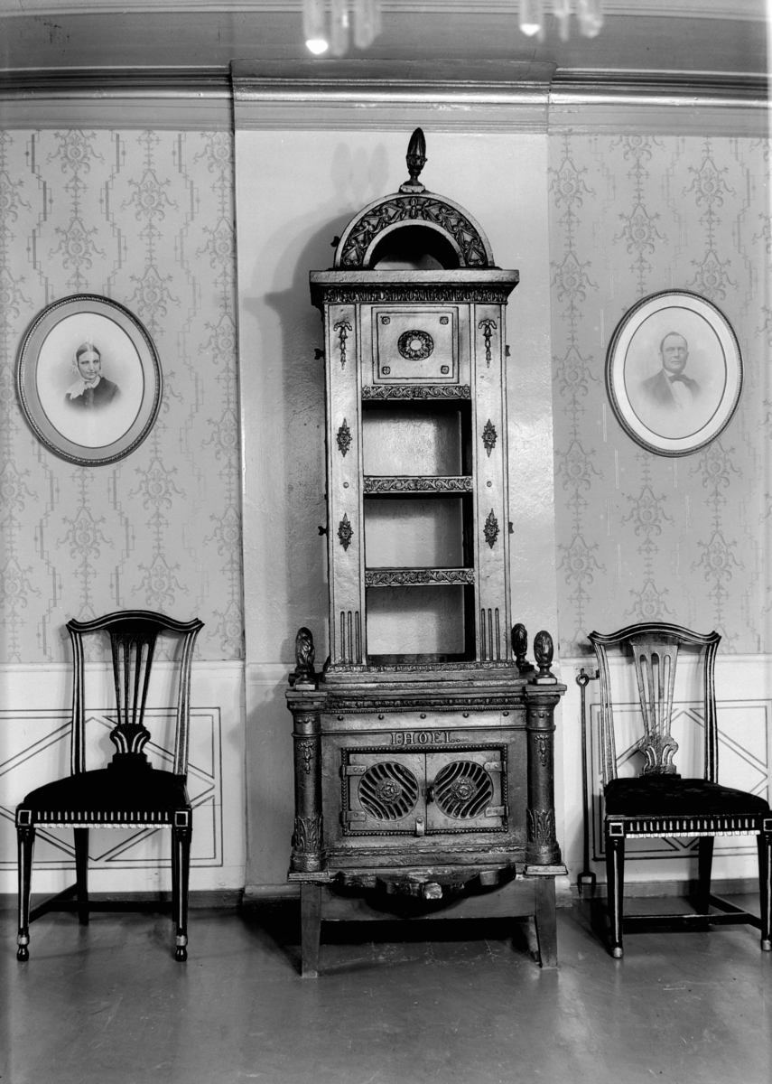 Hovelsrud, Helgøya. Stueinteriør med stoler og empireovn. Portretter på ...