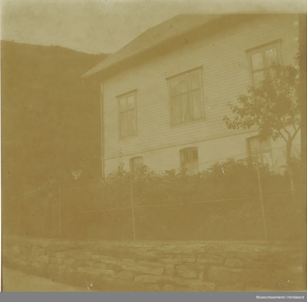 amatørfotografi av kvitt hus med hage over ein mur med gjerde på ...